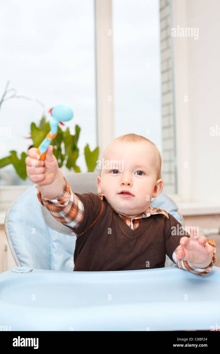 Little kid sitting in highchair and waving his spoon. Expression during ...