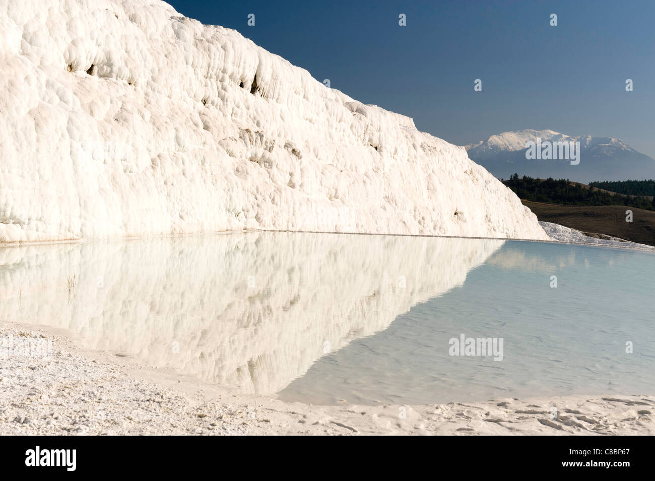 A snow capped mountain is reflected in a travertine at Pamukkale ...