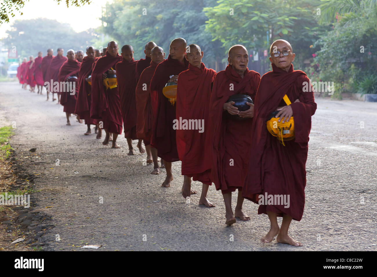 Monks walking for morning alms barefoot in street holding rice bowls ...