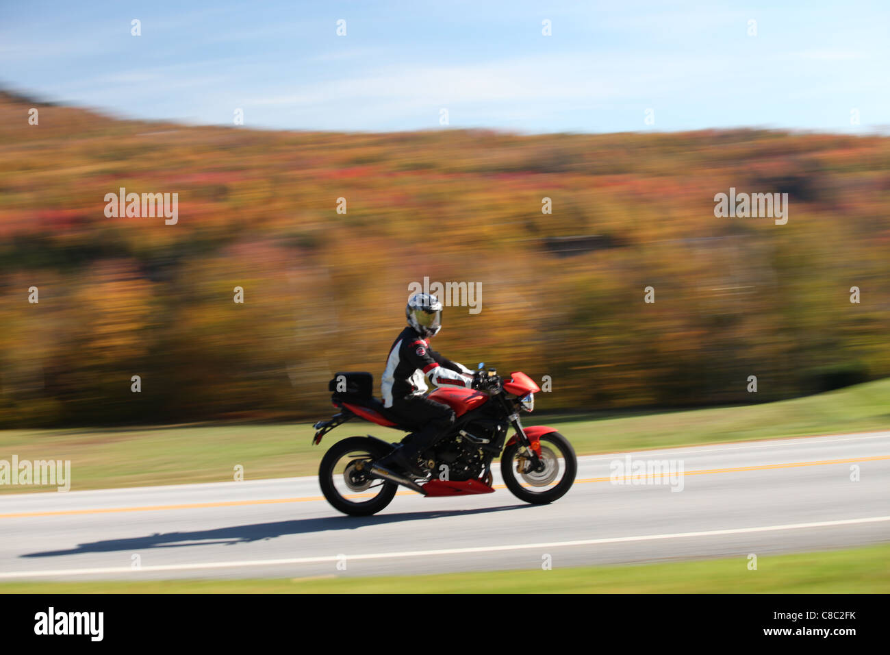 Motorcycle speeds through vibrant fall foliage on highway in Vermont ...