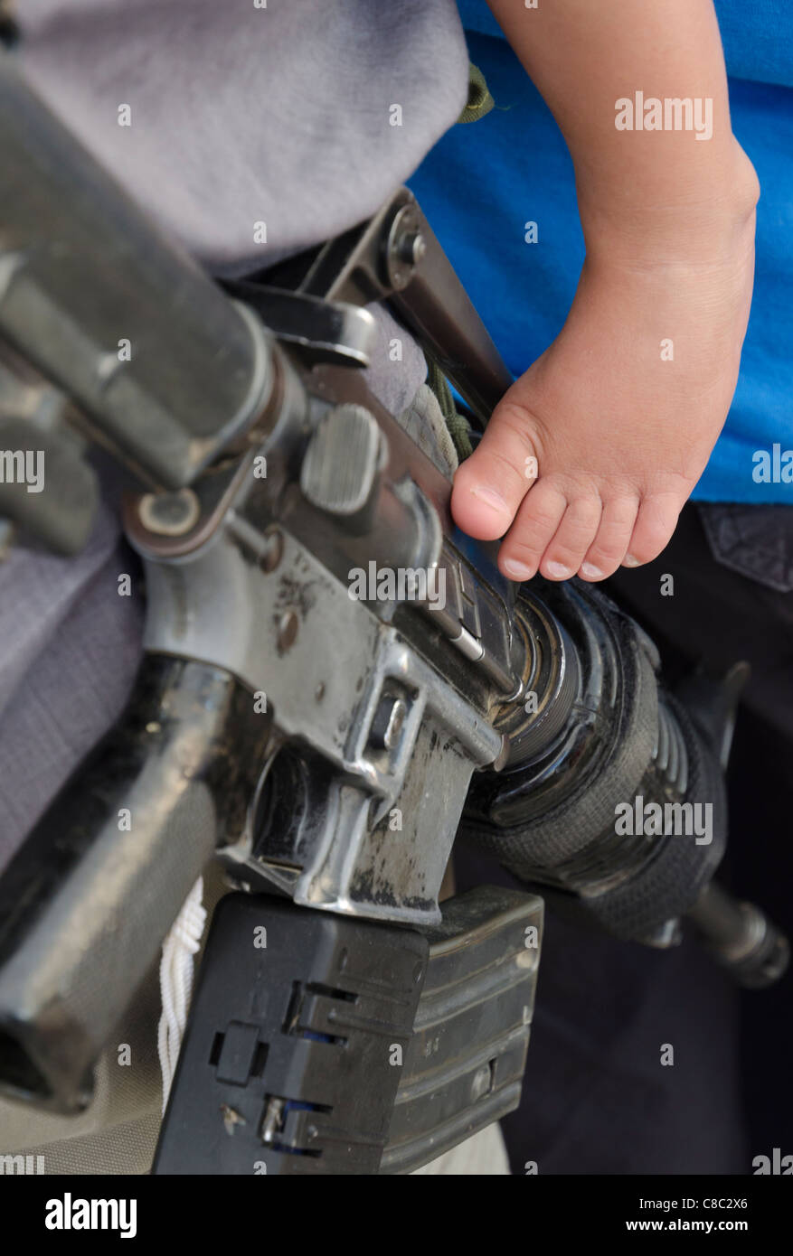close up of toddlers foot and gun hanging from sttlers shouldre ...