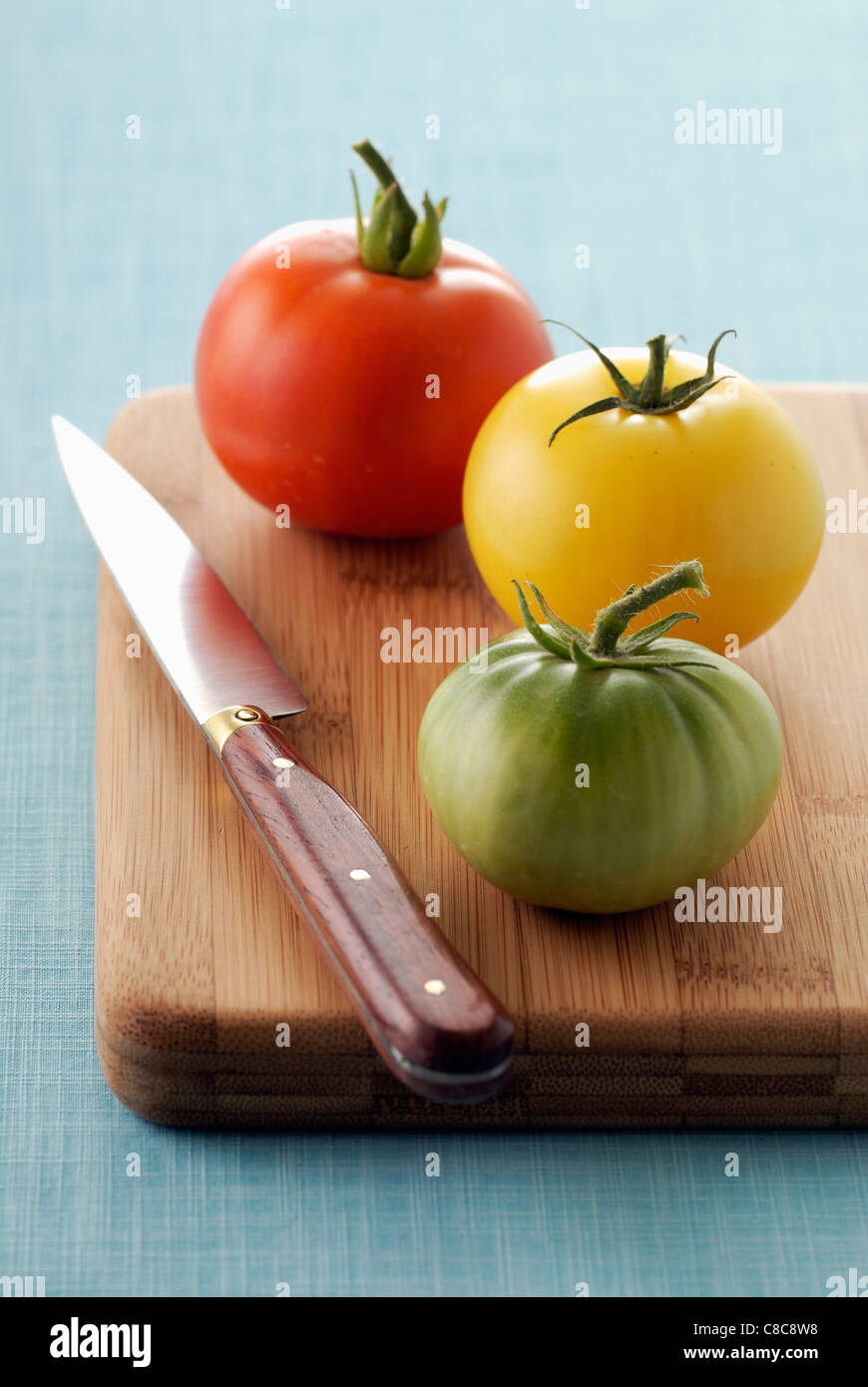 Three different coloured tomatoes on a chopping board Stock Photo - Alamy