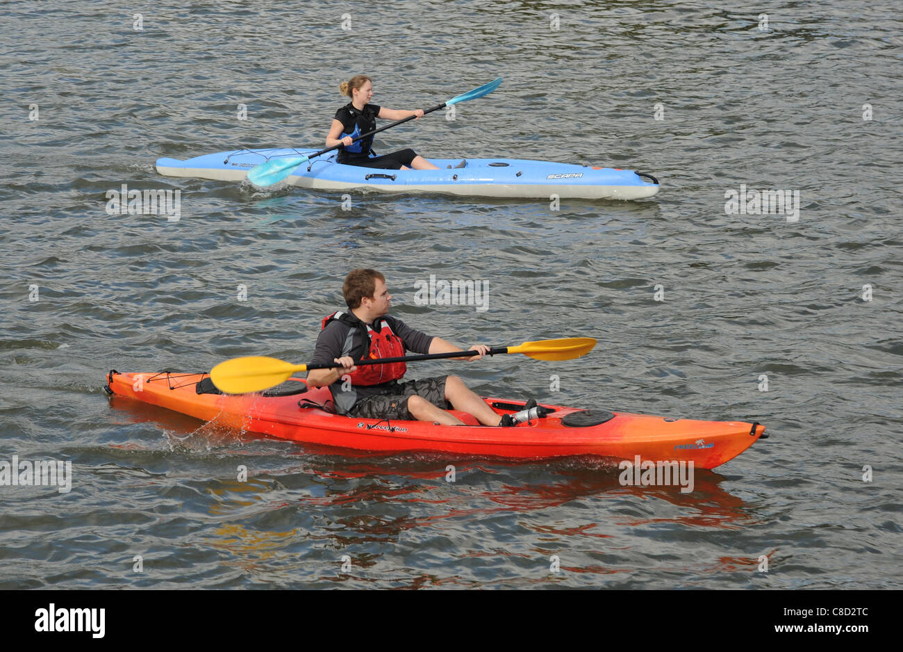 A man and a woman kayaking together. orange and blue kayaks, rippled ...