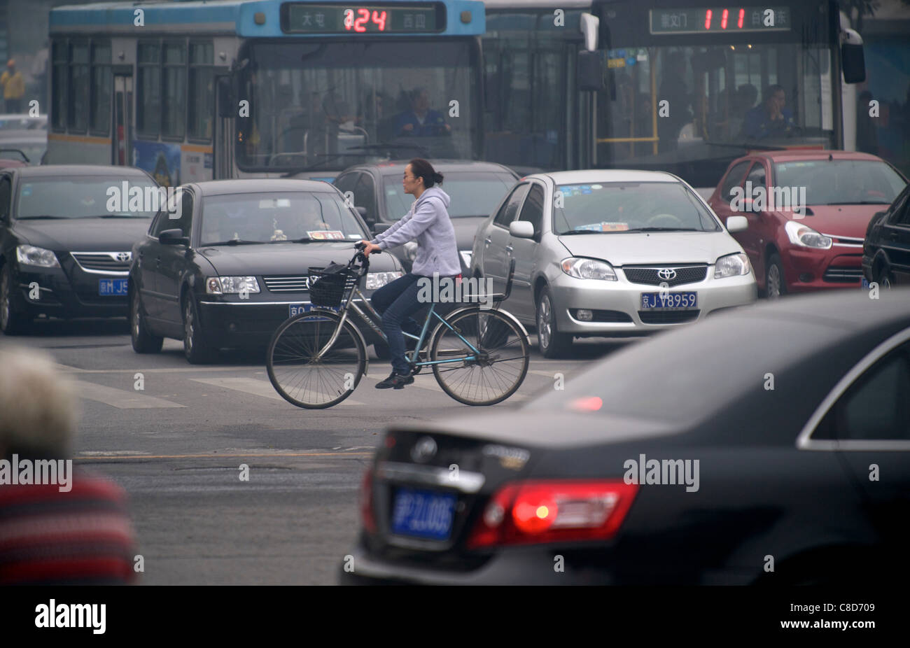 A Chinese woman rides a bicycle among vehicles in an air-polluted ...