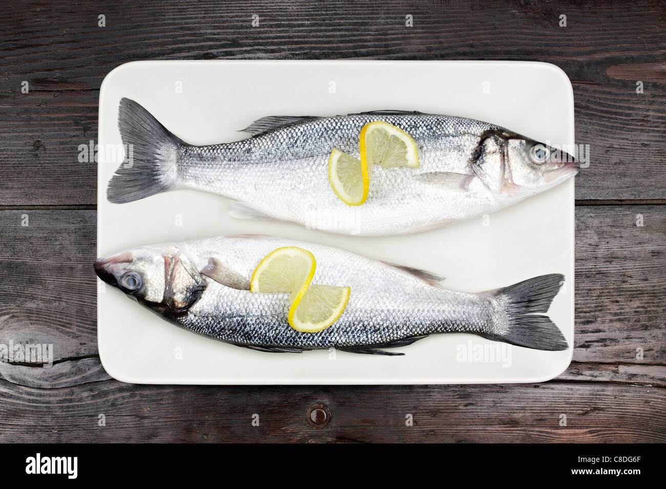 Fresh sea bass in a white plate, on a wooden surface Stock Photo - Alamy
