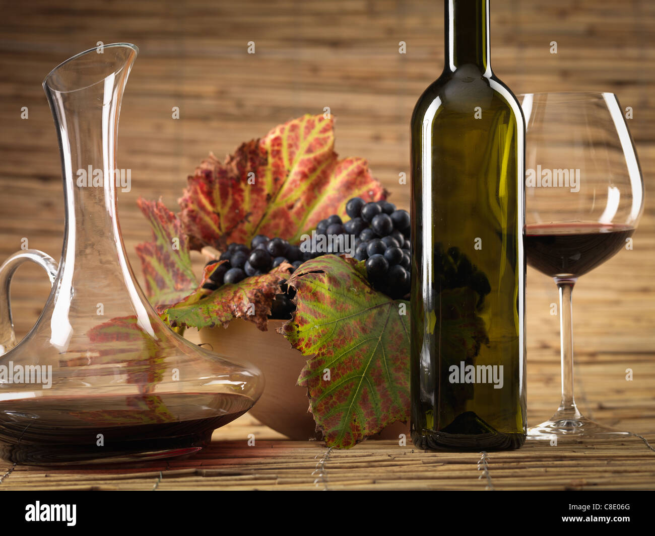 bottle of red wine, glass, pitcher and grapes on wicker background ...