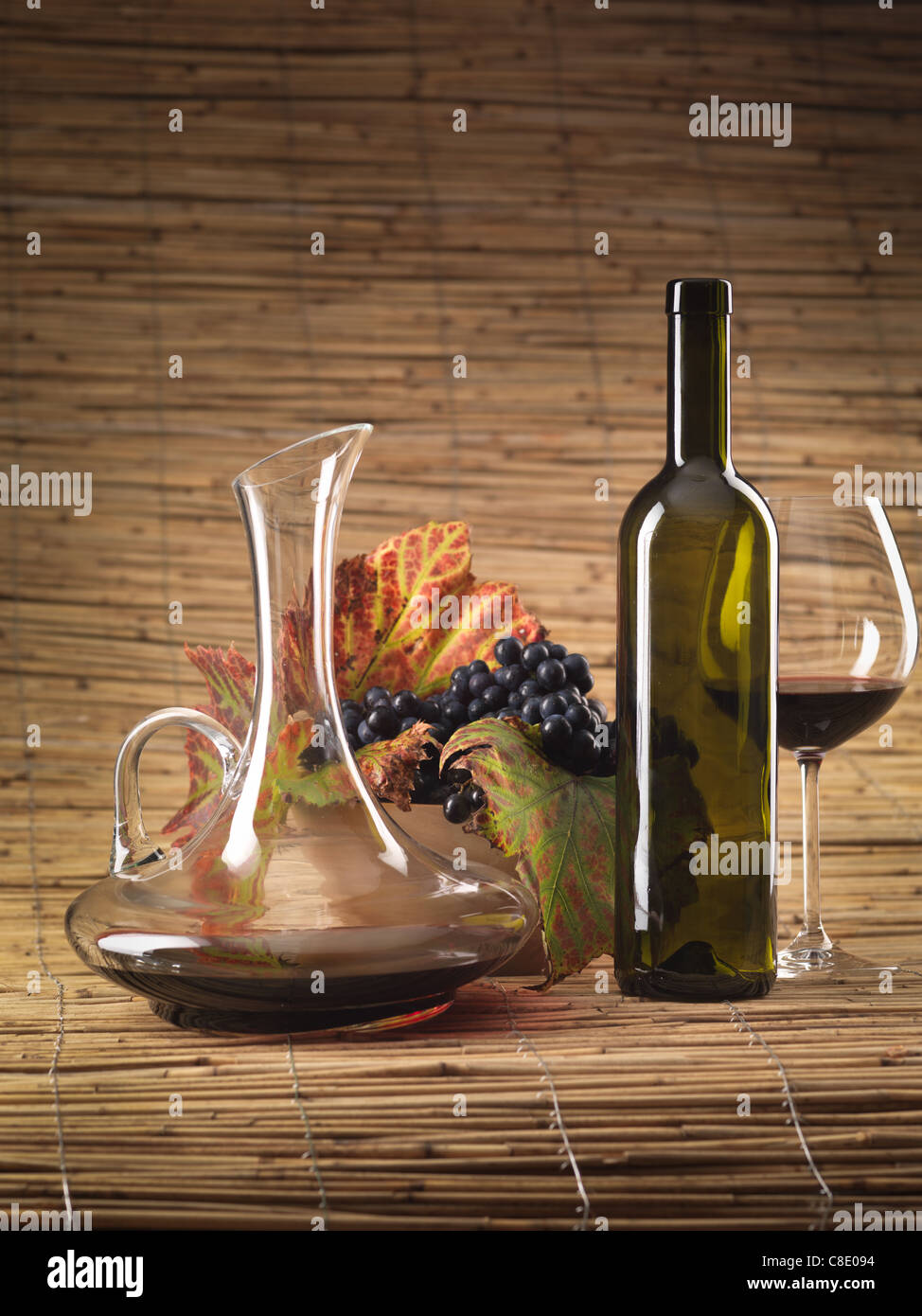 bottle of red wine, glass, pitcher and grapes on wicker background ...