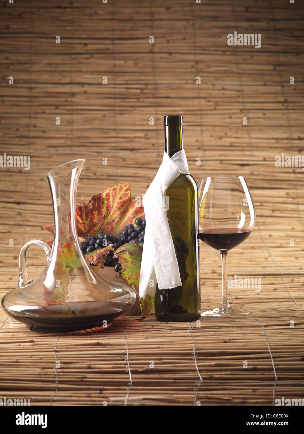 bottle of red wine, glass, pitcher and grapes on wicker background ...
