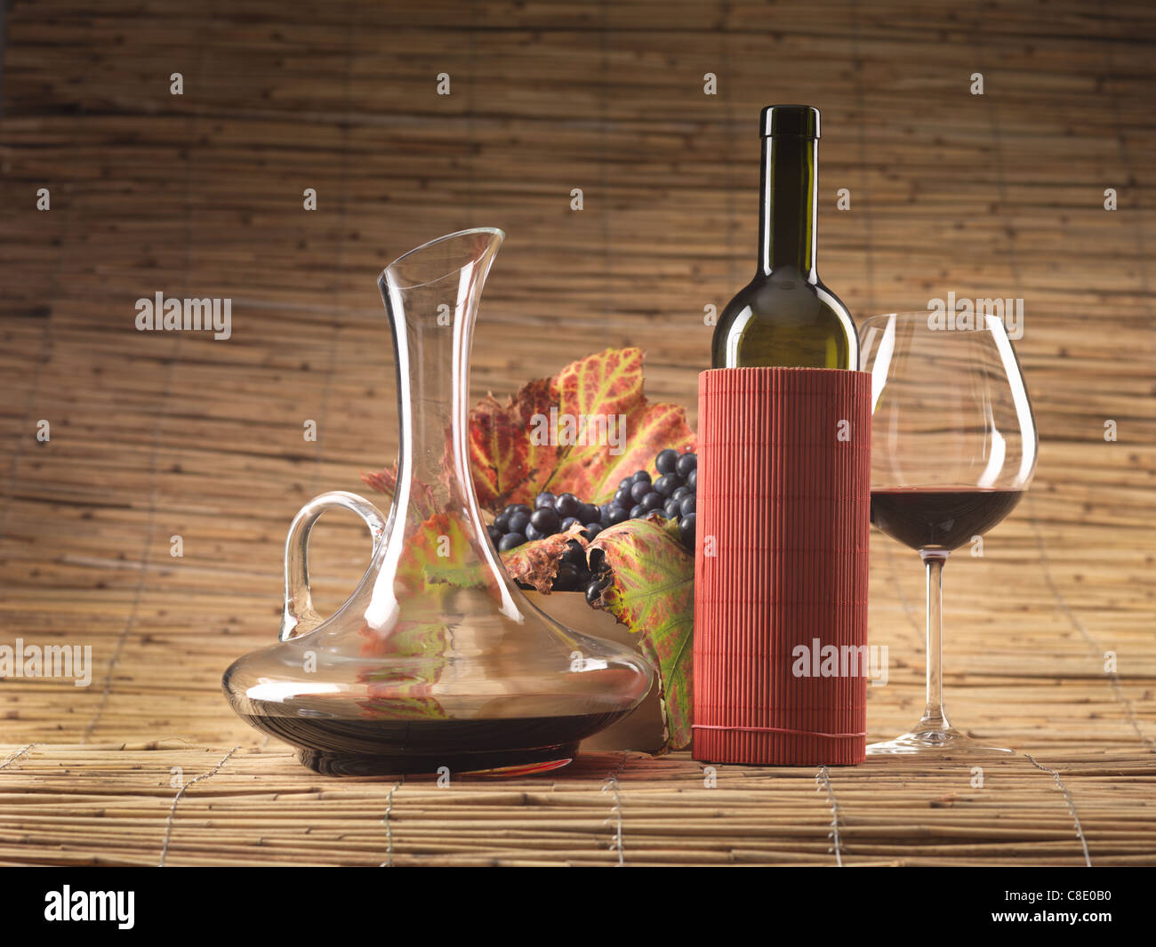 bottle of red wine, glass, pitcher and grapes on wicker background ...