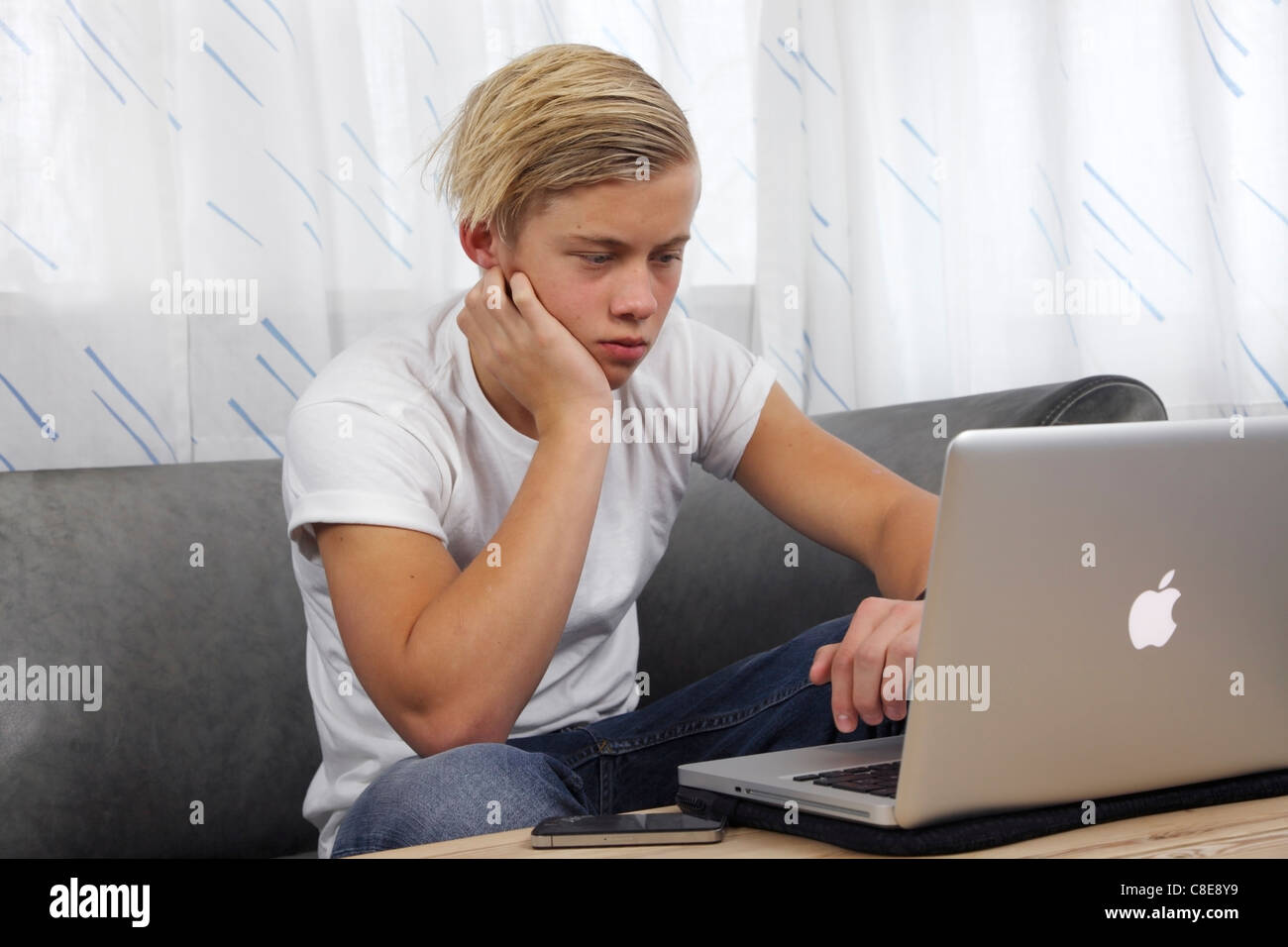 Male teenager using his Apple MacBook Pro for homework while keeping ...