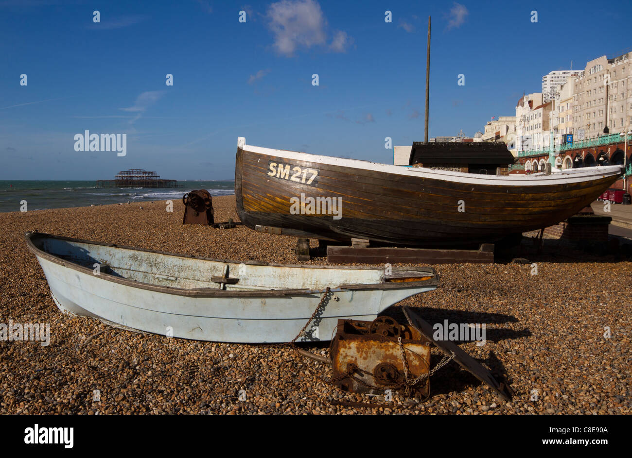 Boats on a pebble beach on Brighton Seafront with the burn out shell on ...