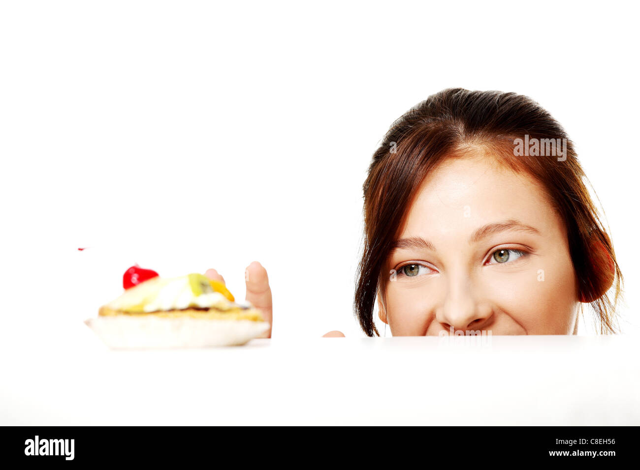 Young caucasian girl hiding behing the desk and reaching for the cake ...