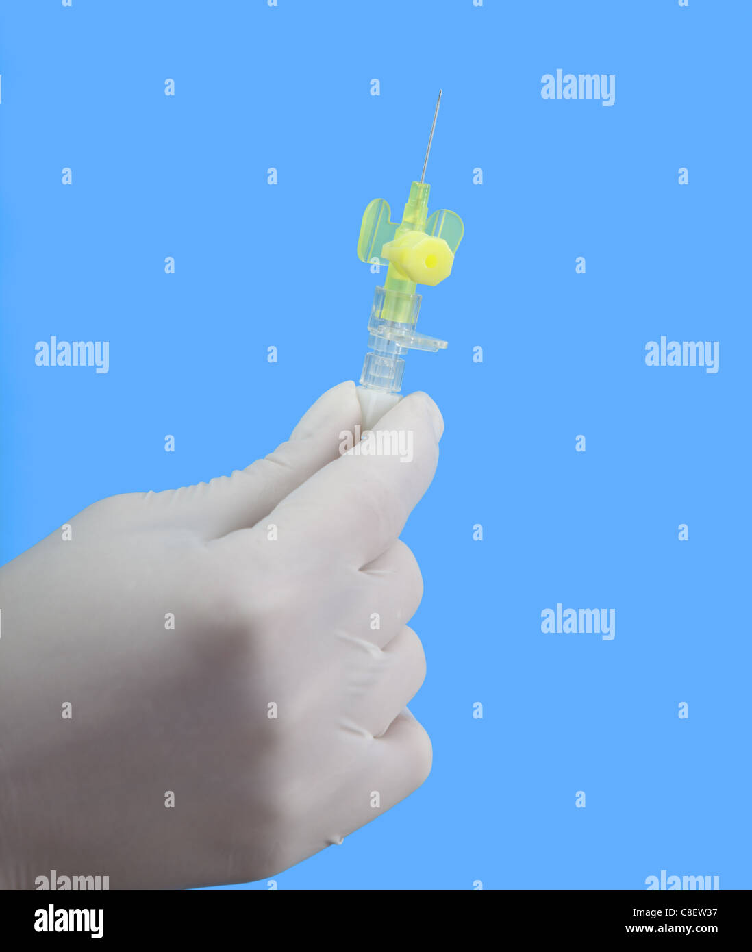 Hand in surgical glove holding a small intravenous needle against a ...