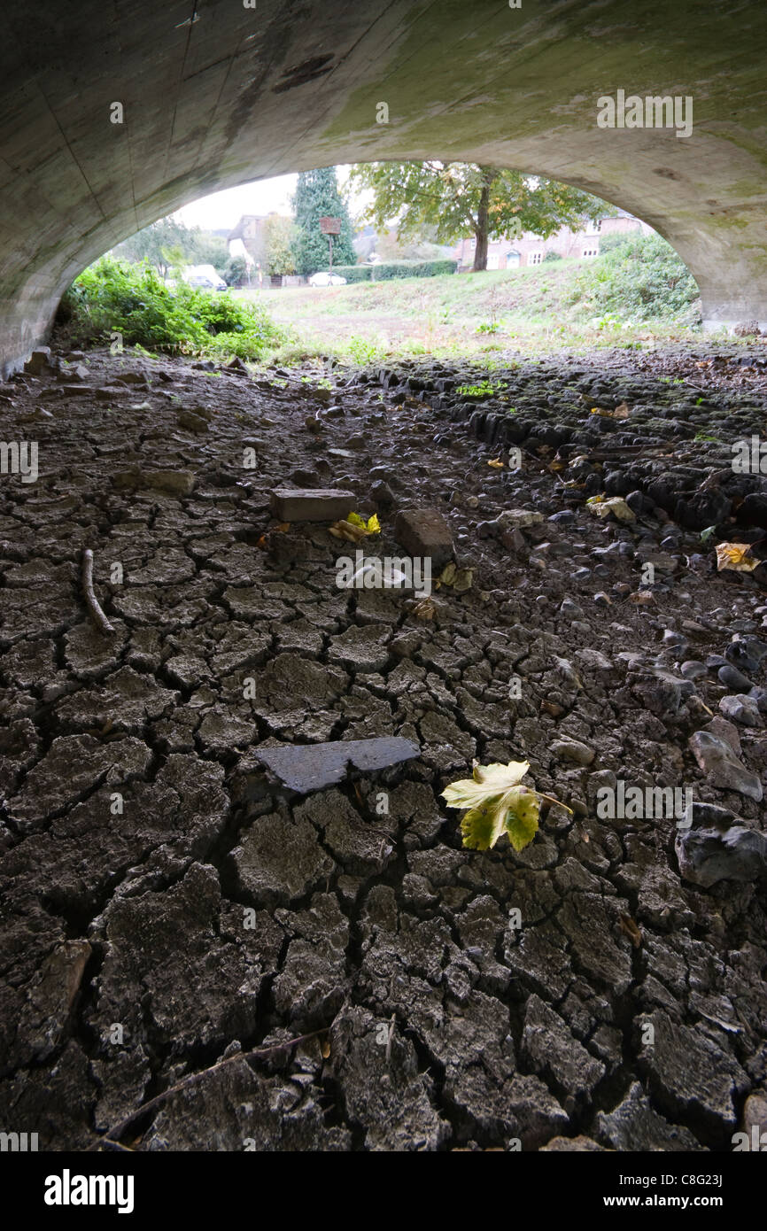 A dry river in Autumn showing cracked mud. The bridge gives an idea of ...