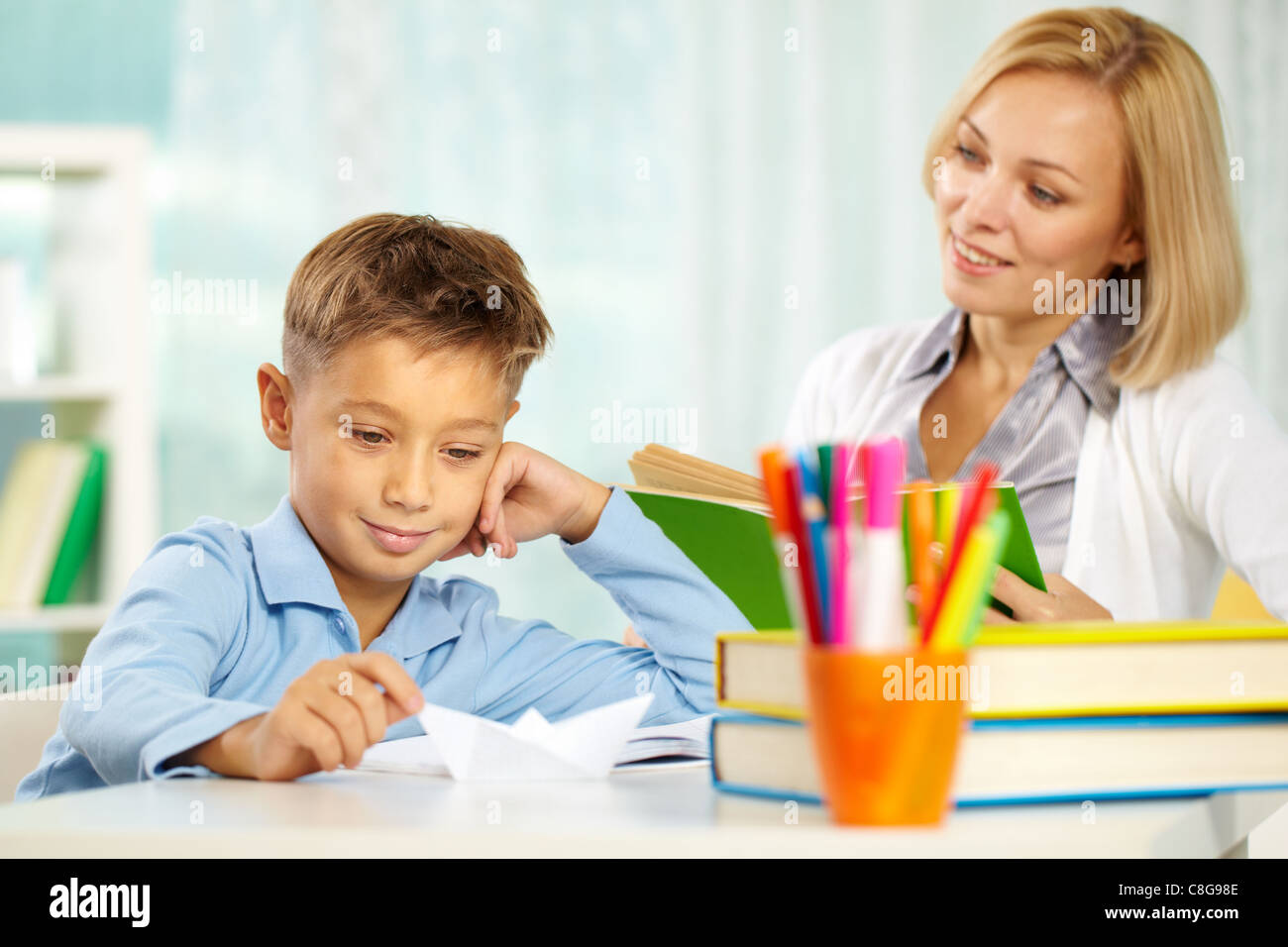 Portrait of handsome boy at workplace with his tutor sitting near by ...