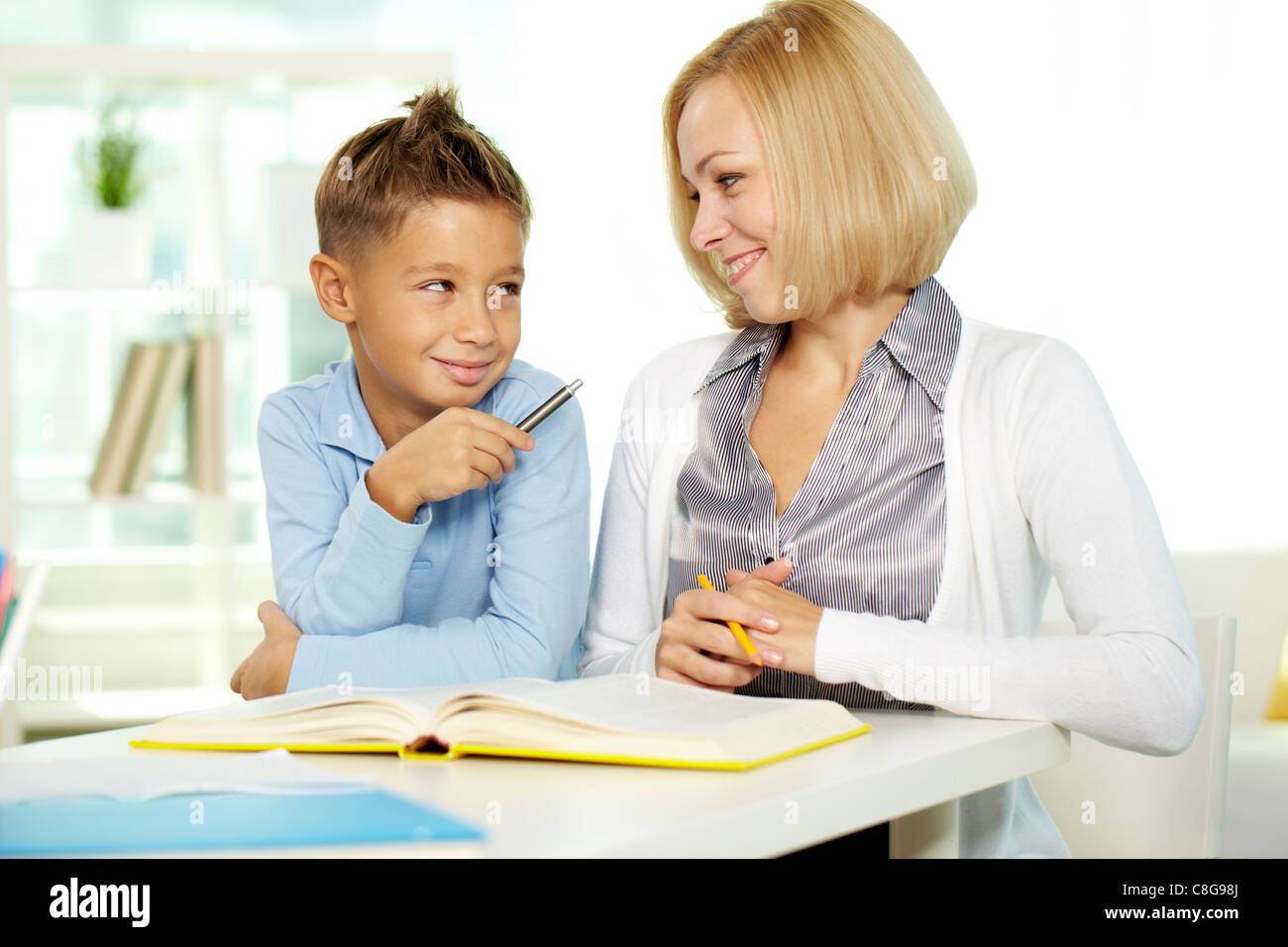 Portrait of pretty tutor and diligent pupil looking at each other while ...
