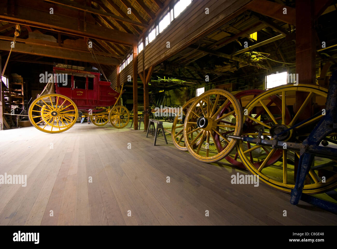 A stagecoach and wagon-wheels await repair in a maintenance workshop ...