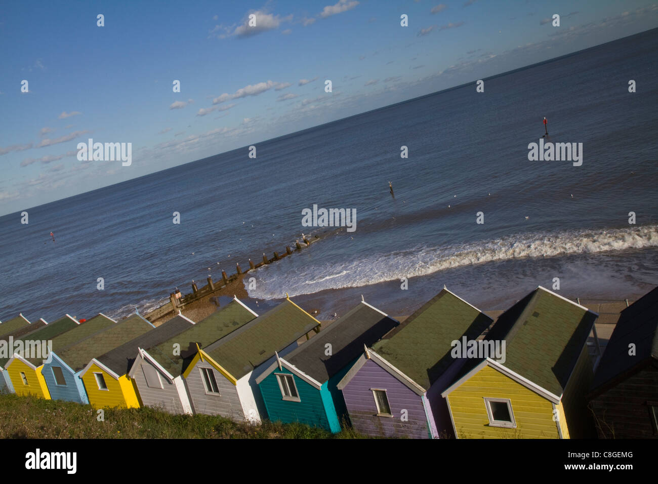 Colourful beach huts look out over the sea under a bright blue sky at ...