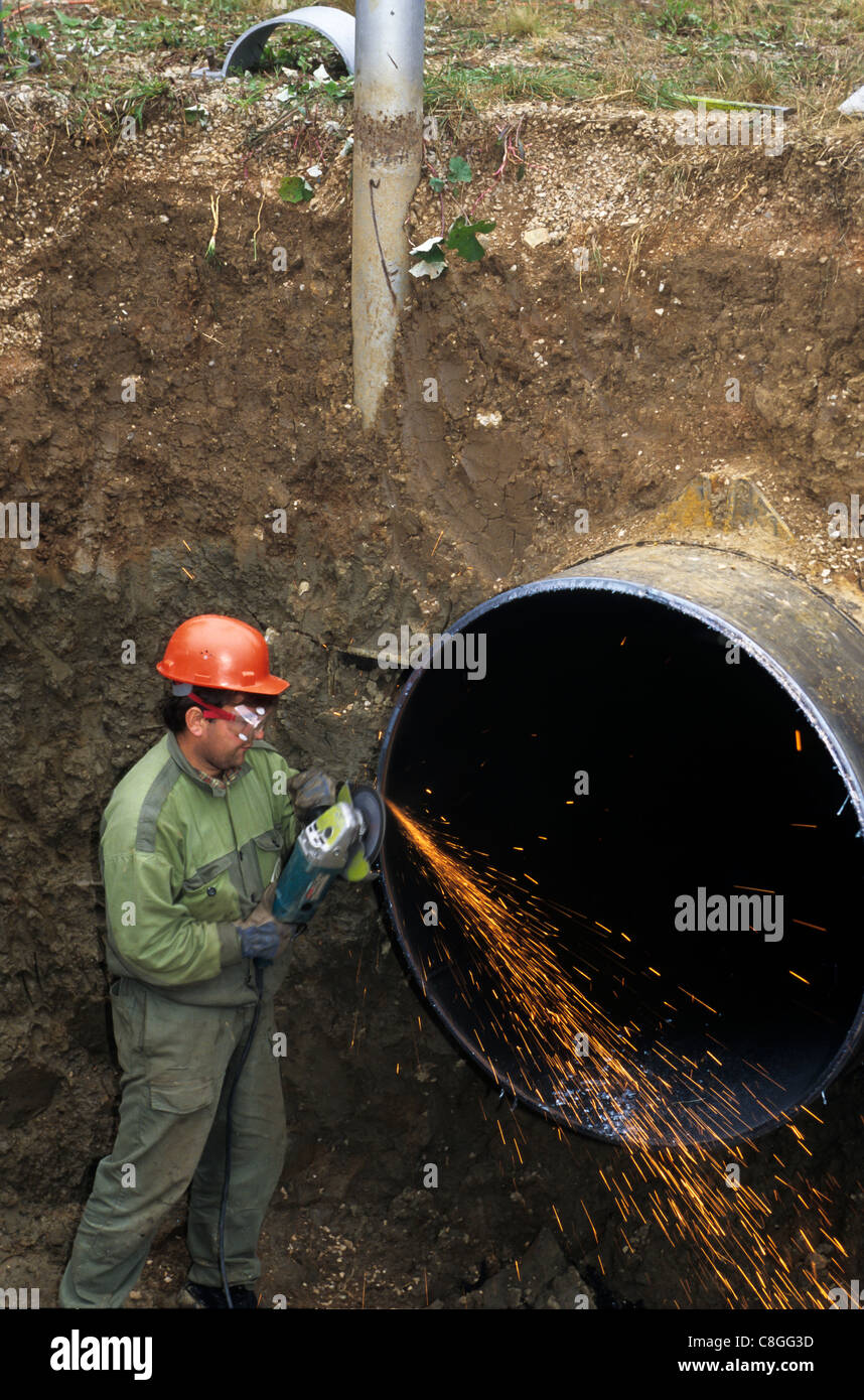 Slovakia. Man wearing an orange hard hat in an excavated hole working ...