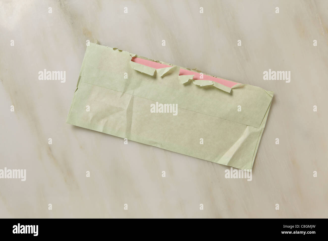A used and slightly torn open green postal envelope on a marble surface ...
