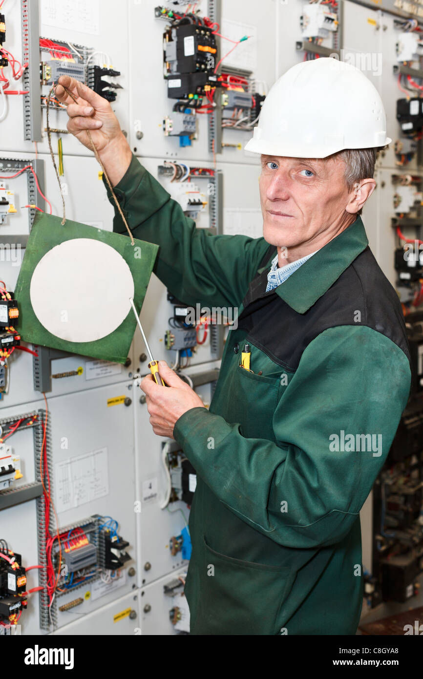 Mature electrician working in white hard hat with cables and wires ...