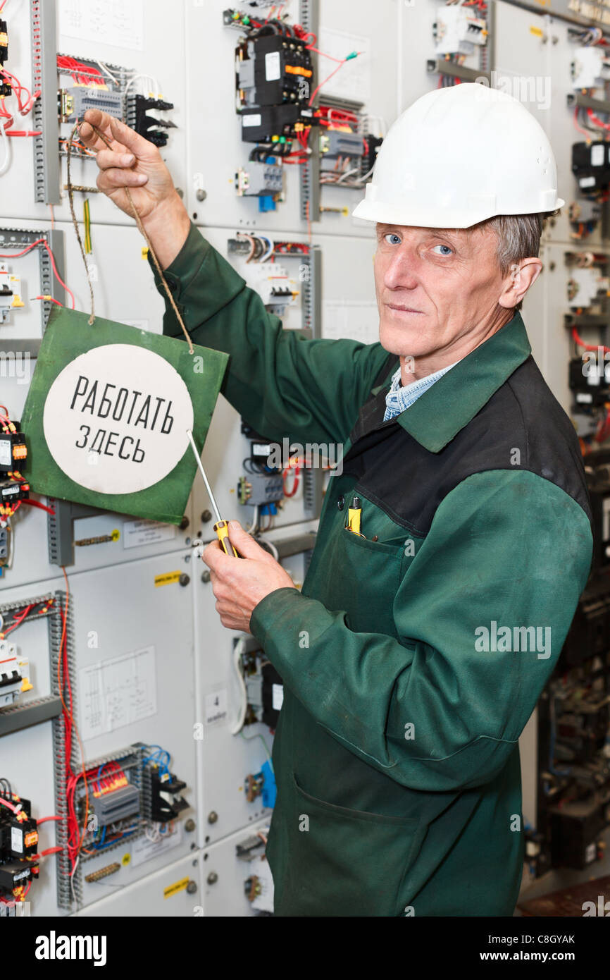 Mature electrician working in white hard hat with cables and wires ...