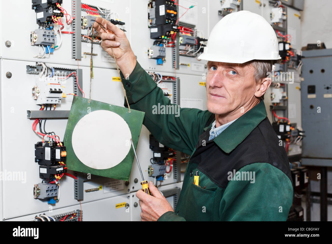 Mature electrician working in white hard hat with cables and wires ...