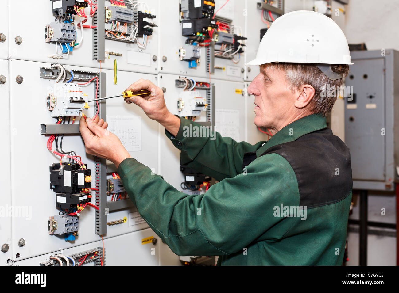 Mature electrician working in white hard hat with cables and wires ...