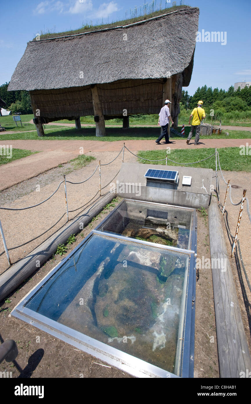 Visitors walk between a burial pit and a reconstruction of a pillar ...