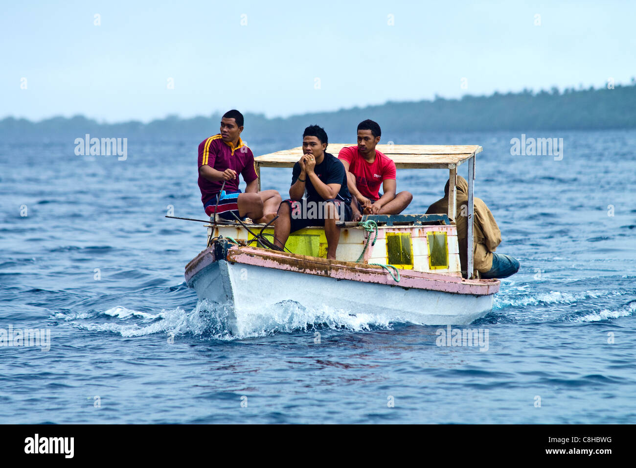 Teenage boys ride on the bow of a small fishing boat between islands ...