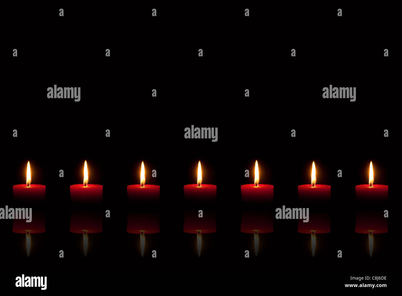 Row of seven burning red candles in front of black background, with ...