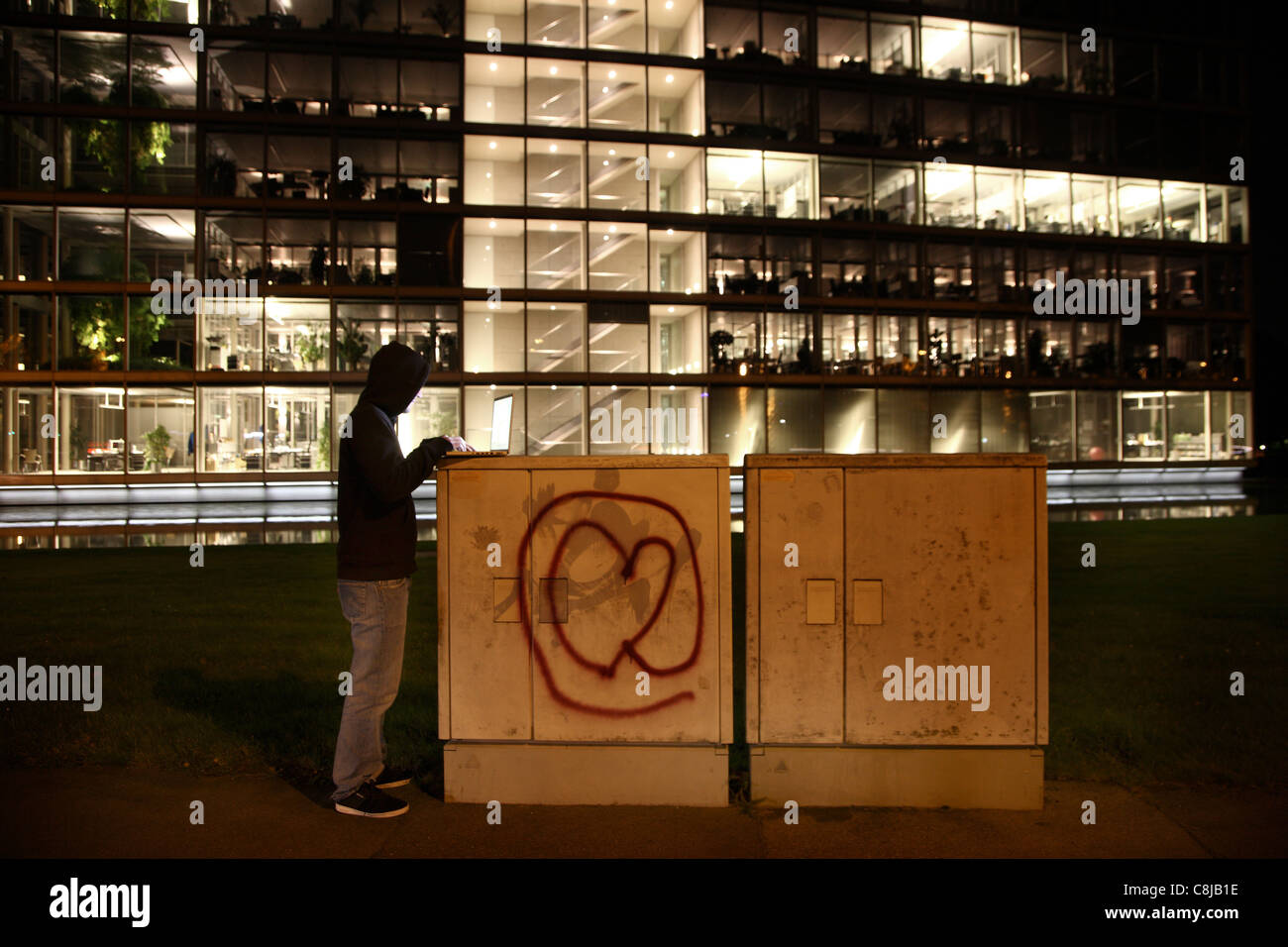 Computer user, hacker, sits conspiratorially, outside, in front of an ...