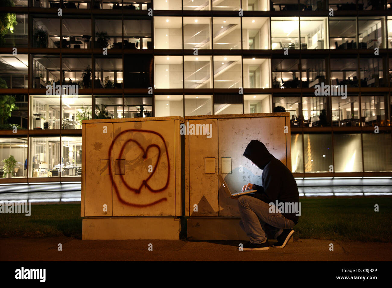 Computer user, hacker, sits conspiratorially, outside, in front of an ...