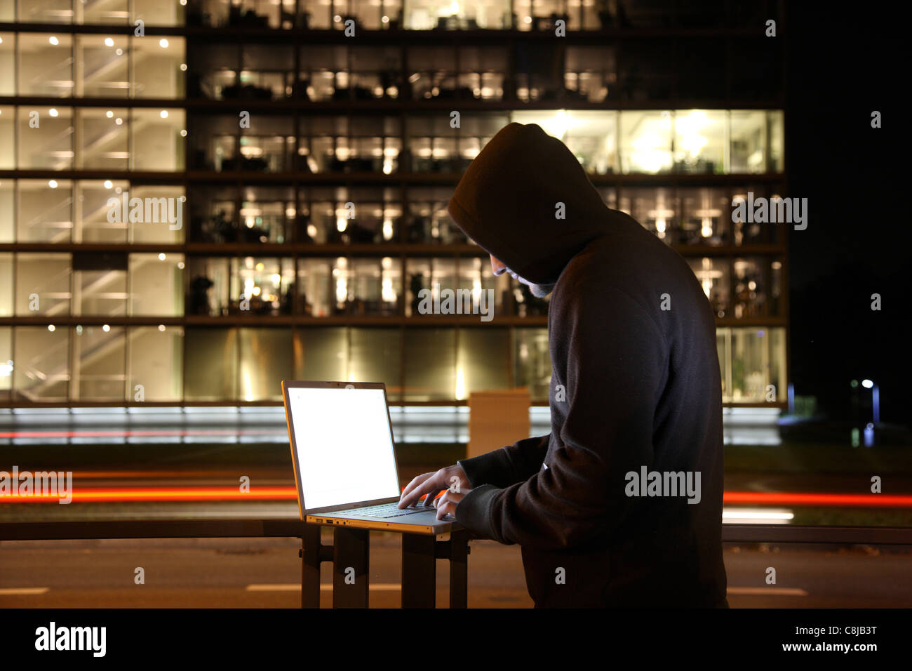 Computer user, hacker, sits conspiratorially, outside, in front of an ...