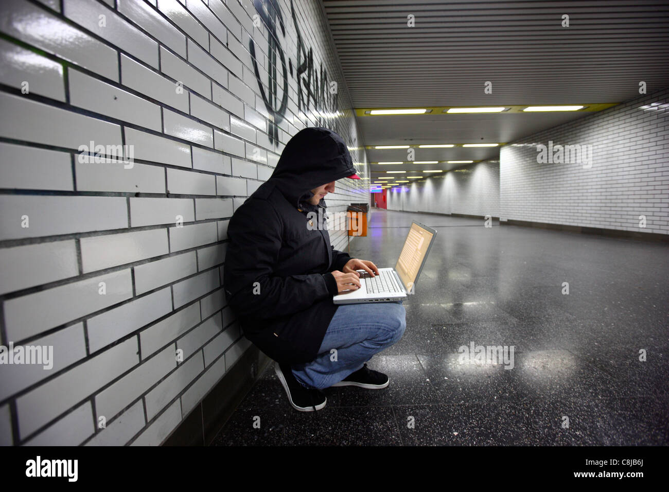 Computer user, hacker, sits conspiratorially with a laptop, in a subway ...