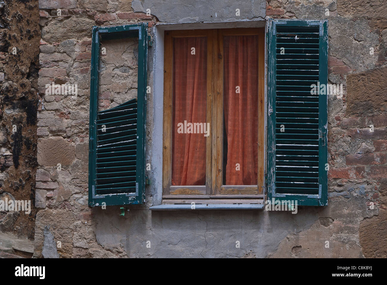 Dilapidated green shutters falling apart on a window with red-orange ...