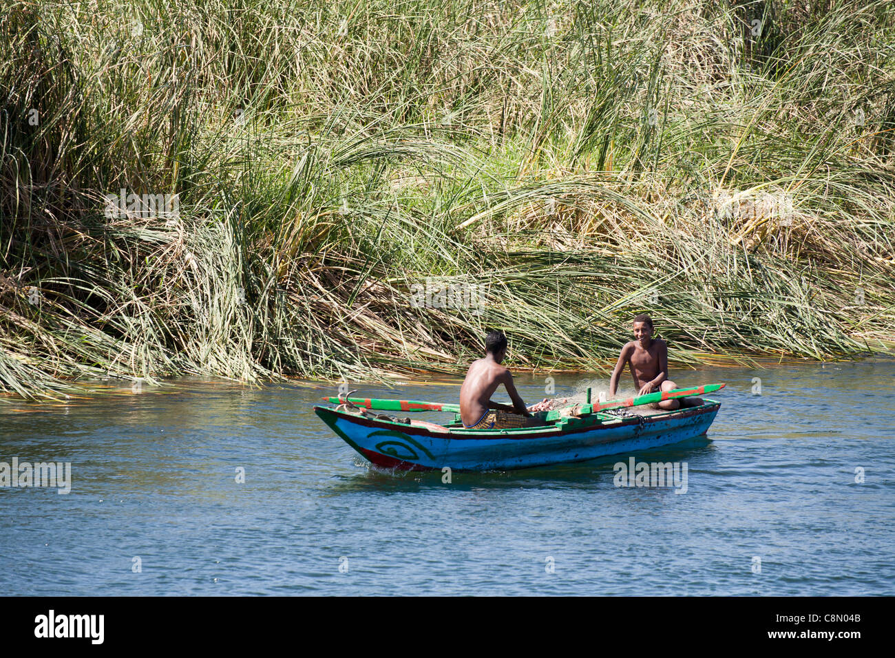 Two young boys rowing a blue painted fishing boat on the river Nile ...