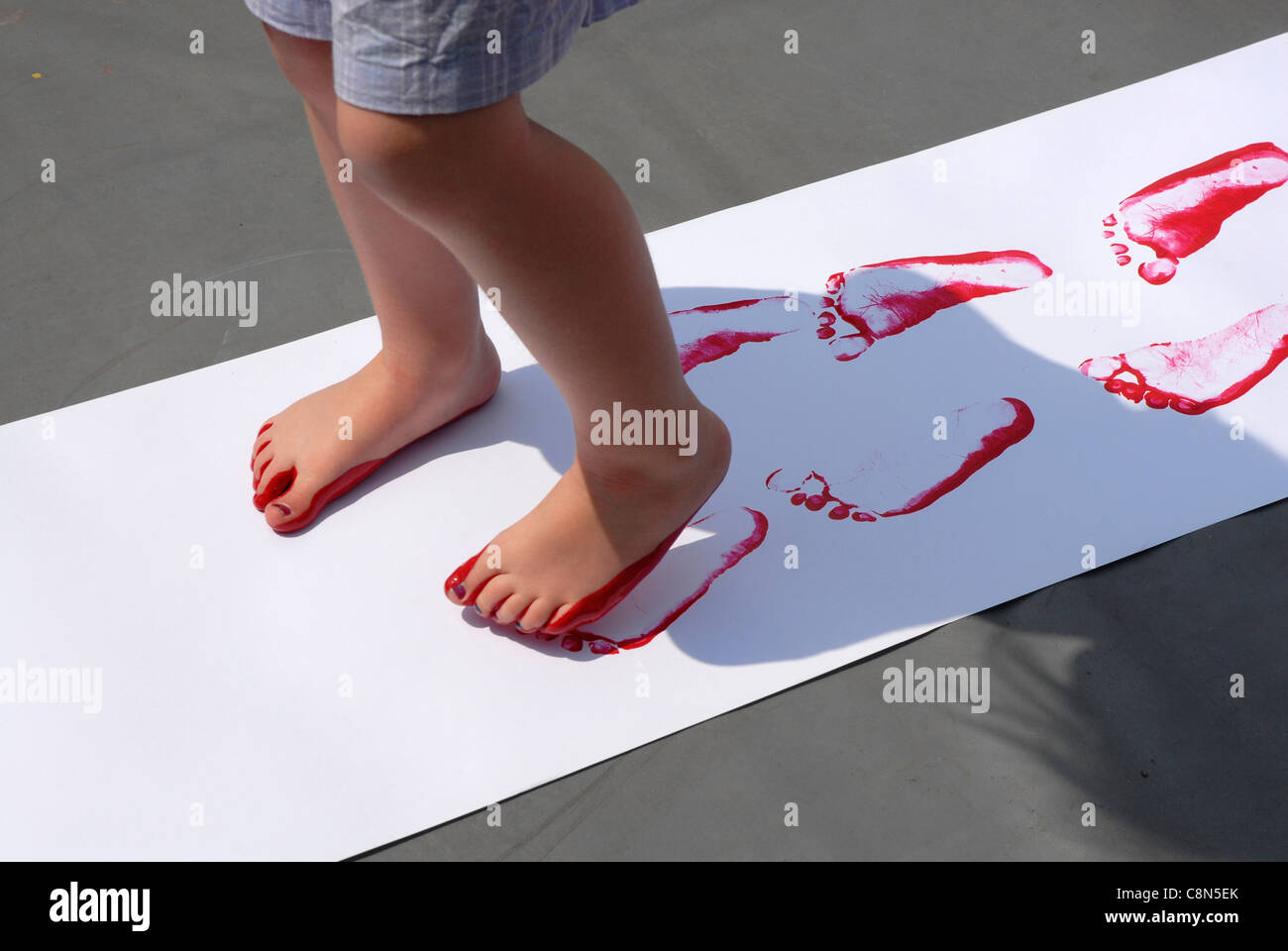 Nursery child painting footprints by walking in paint with bare feet ...