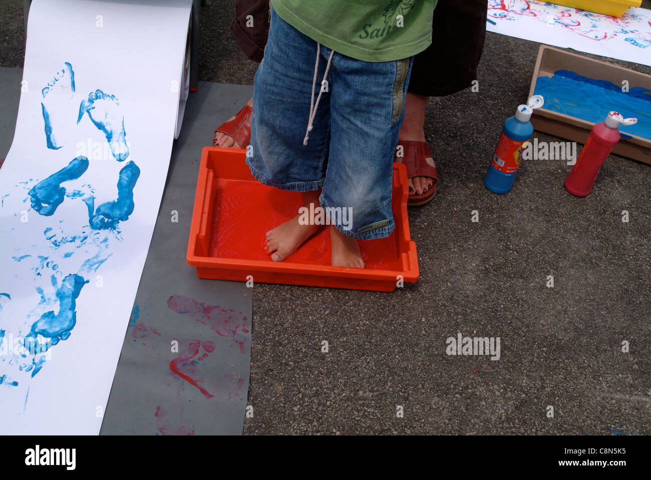Nursery child painting footprints by walking in paint with bare feet ...