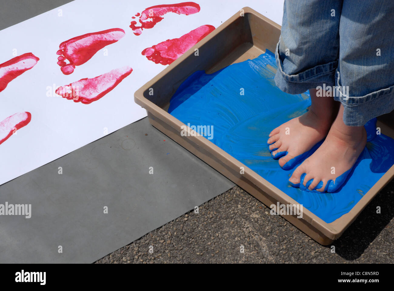 Nursery child painting footprints by walking in paint with bare feet ...