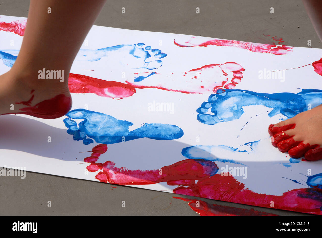 Nursery child painting footprints by walking in paint with bare feet ...
