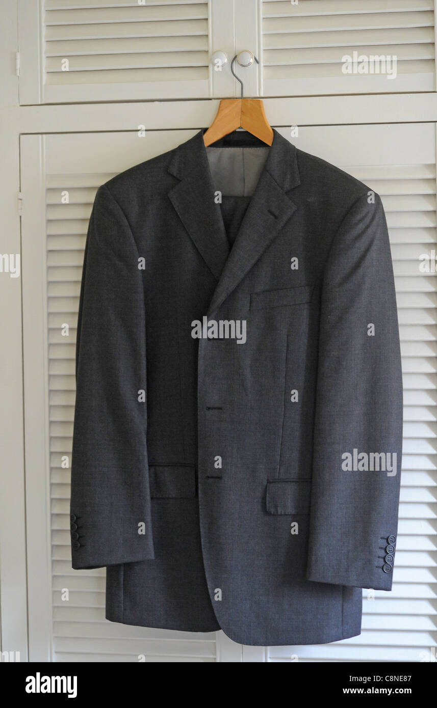 Grey suit with jacket and trousers on a hanger on louvred door wardrobe ...