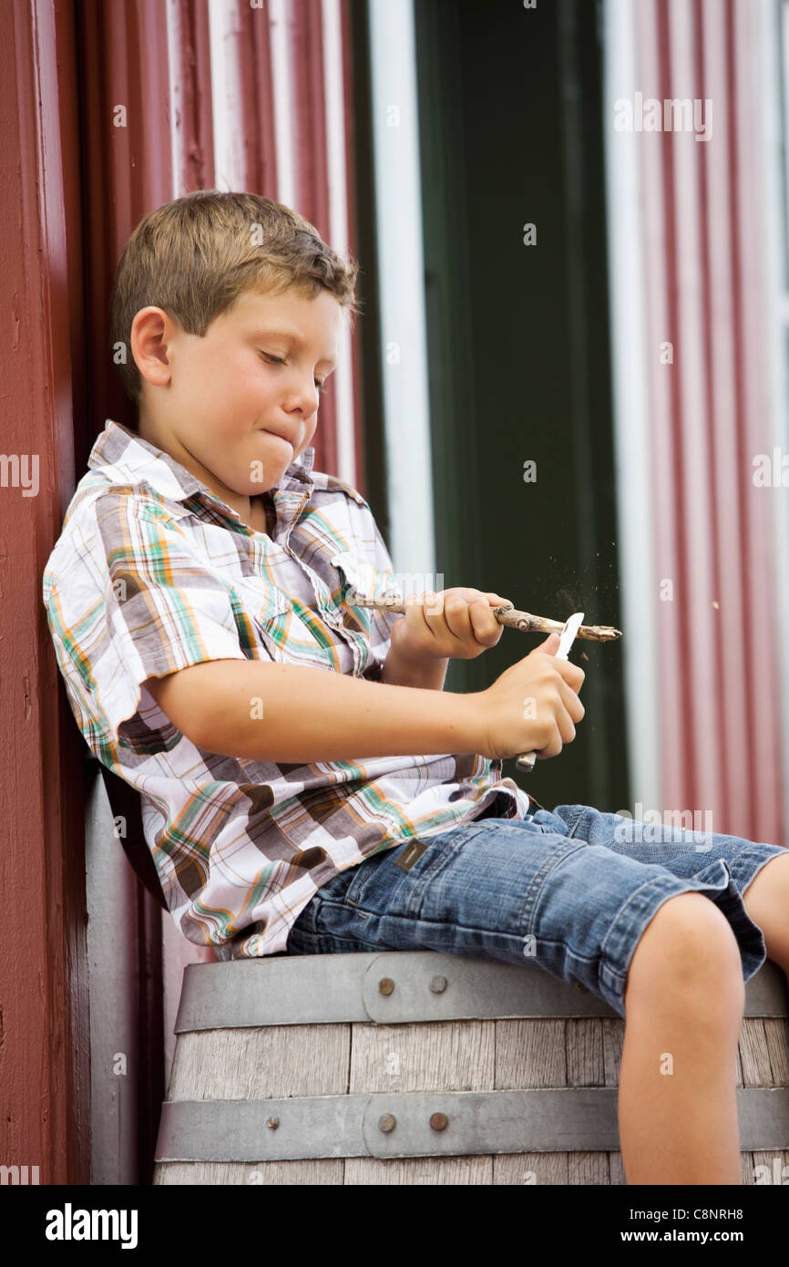 Caucasian boy sitting on barrel whittling stick Stock Photo - Alamy