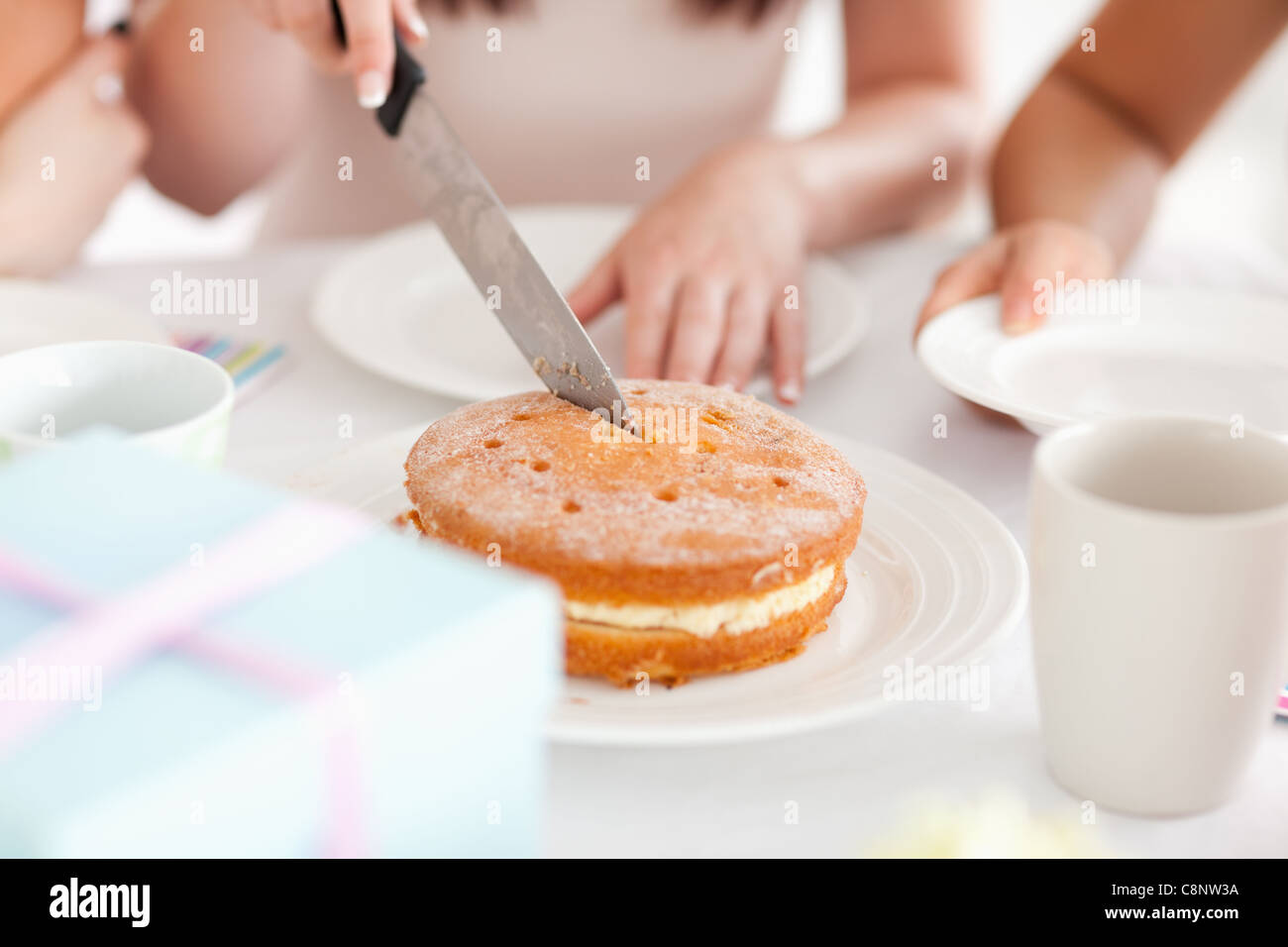 Cute Woman sitting at a table cutting a cake Stock Photo - Alamy