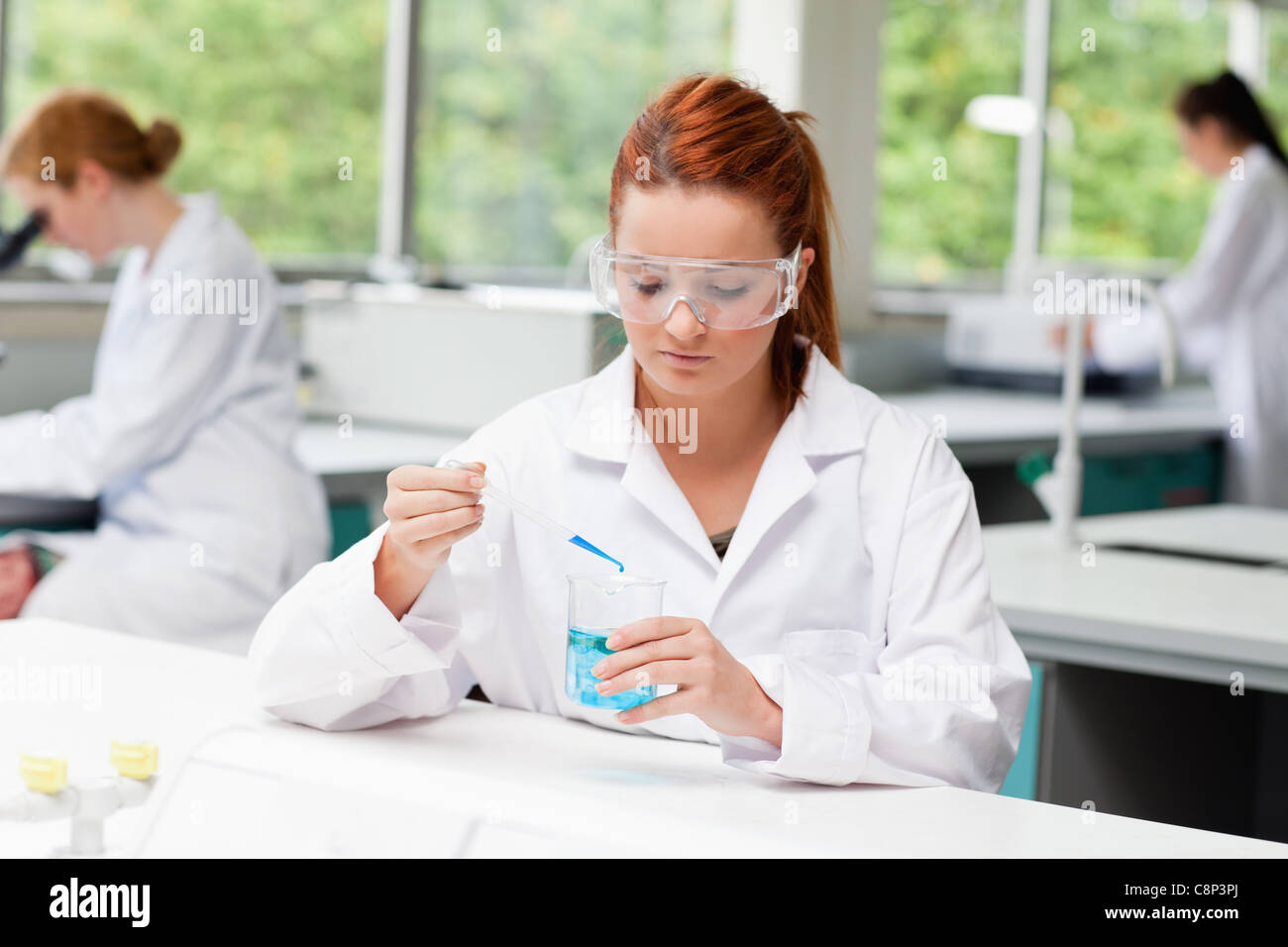 Science student dropping liquid in a beaker while her classmates are ...