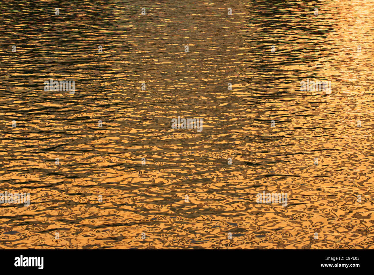 Sunrise adds a golden glow to the ripples in the water Stock Photo - Alamy