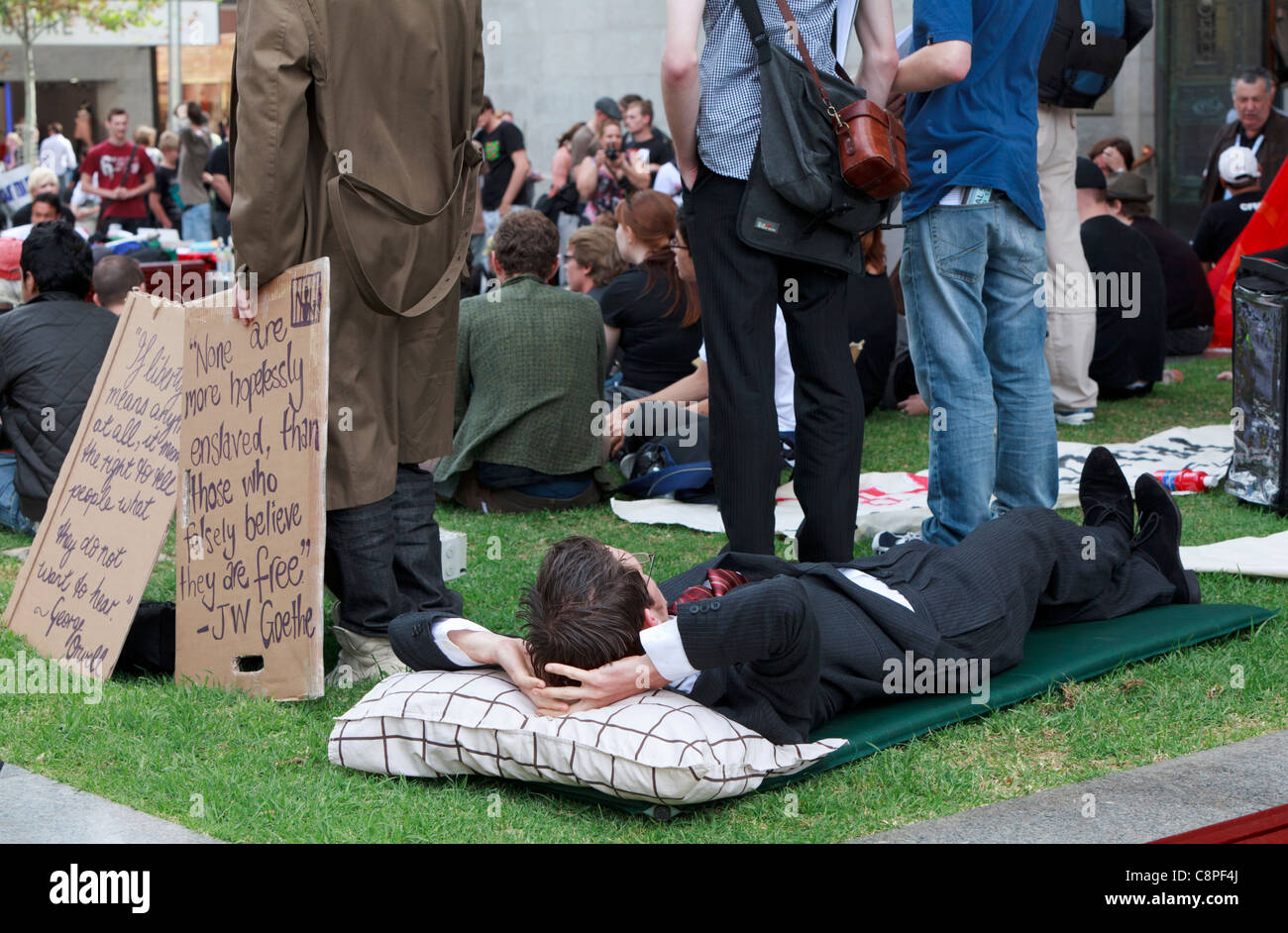 Man in a suit lying down next to man with hand written placards at ...