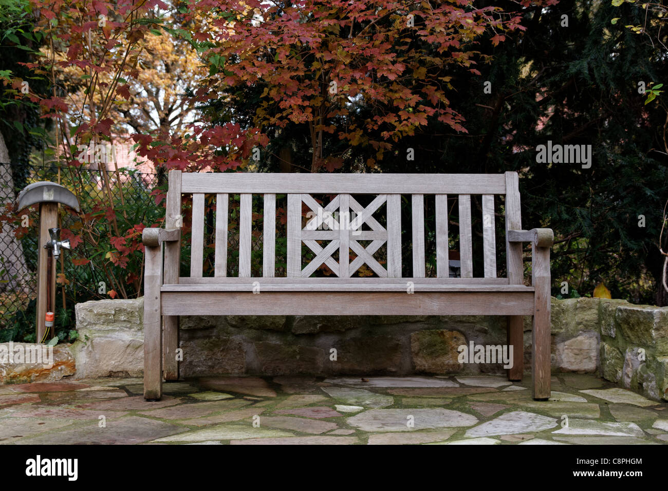 A pale teak wood garden bench on a stone terrace before a background of ...