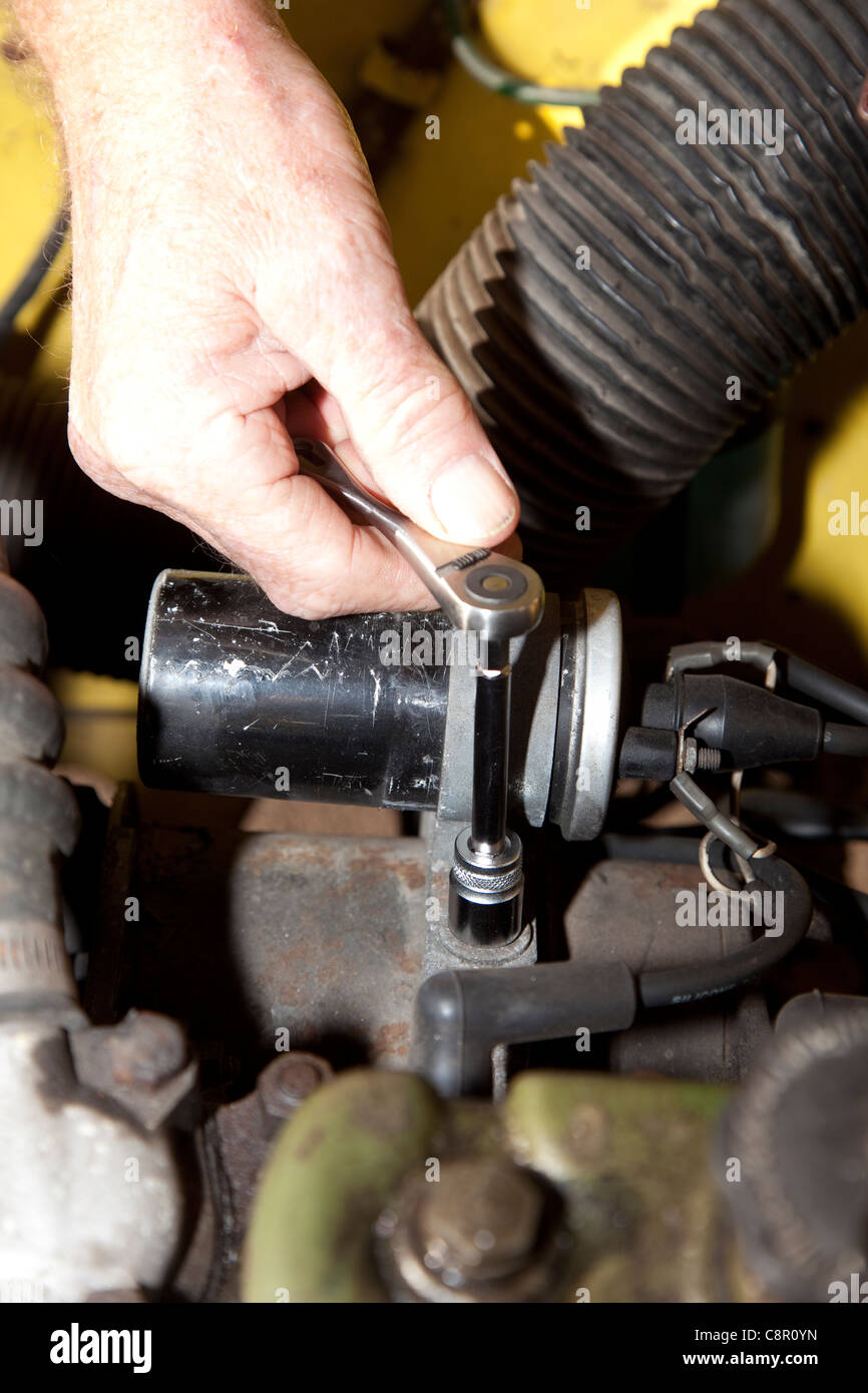 A man uses a socket set in the engine compartment of his yellow Morris ...