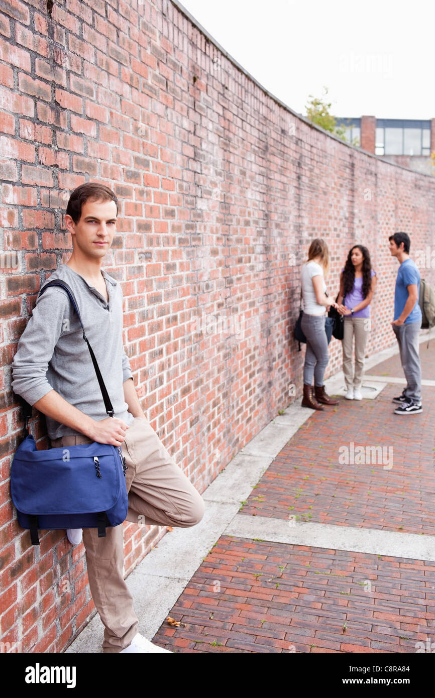 Portrait of a student leaning on a wall while his friends are talking ...